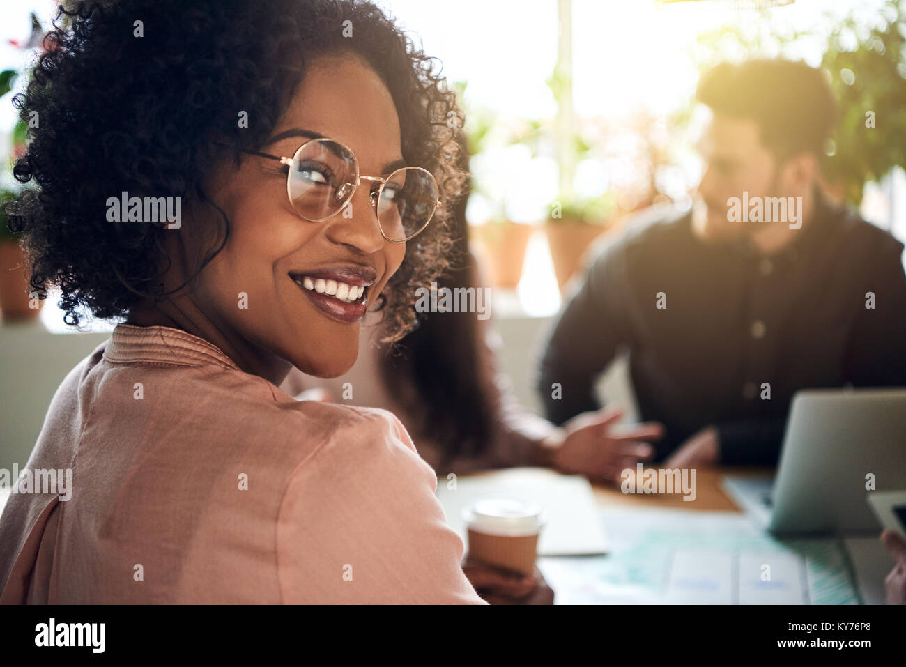 Smiling African businesswoman looking over her shoulder while sitting ...