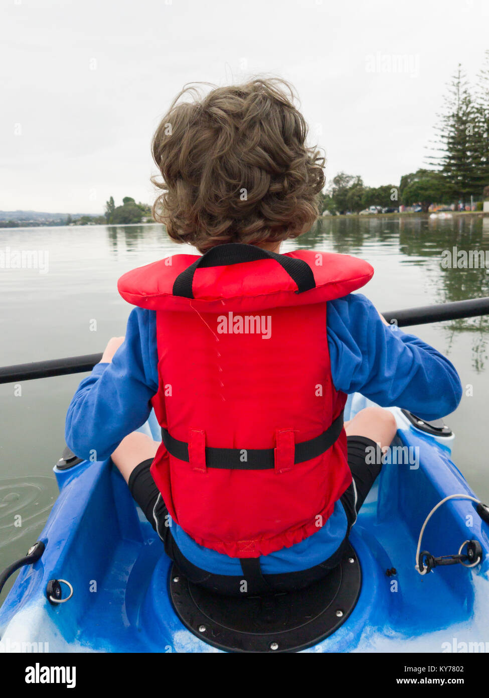 Small boy in red life jacket paddling kayak viewed fro rear Stock Photo ...