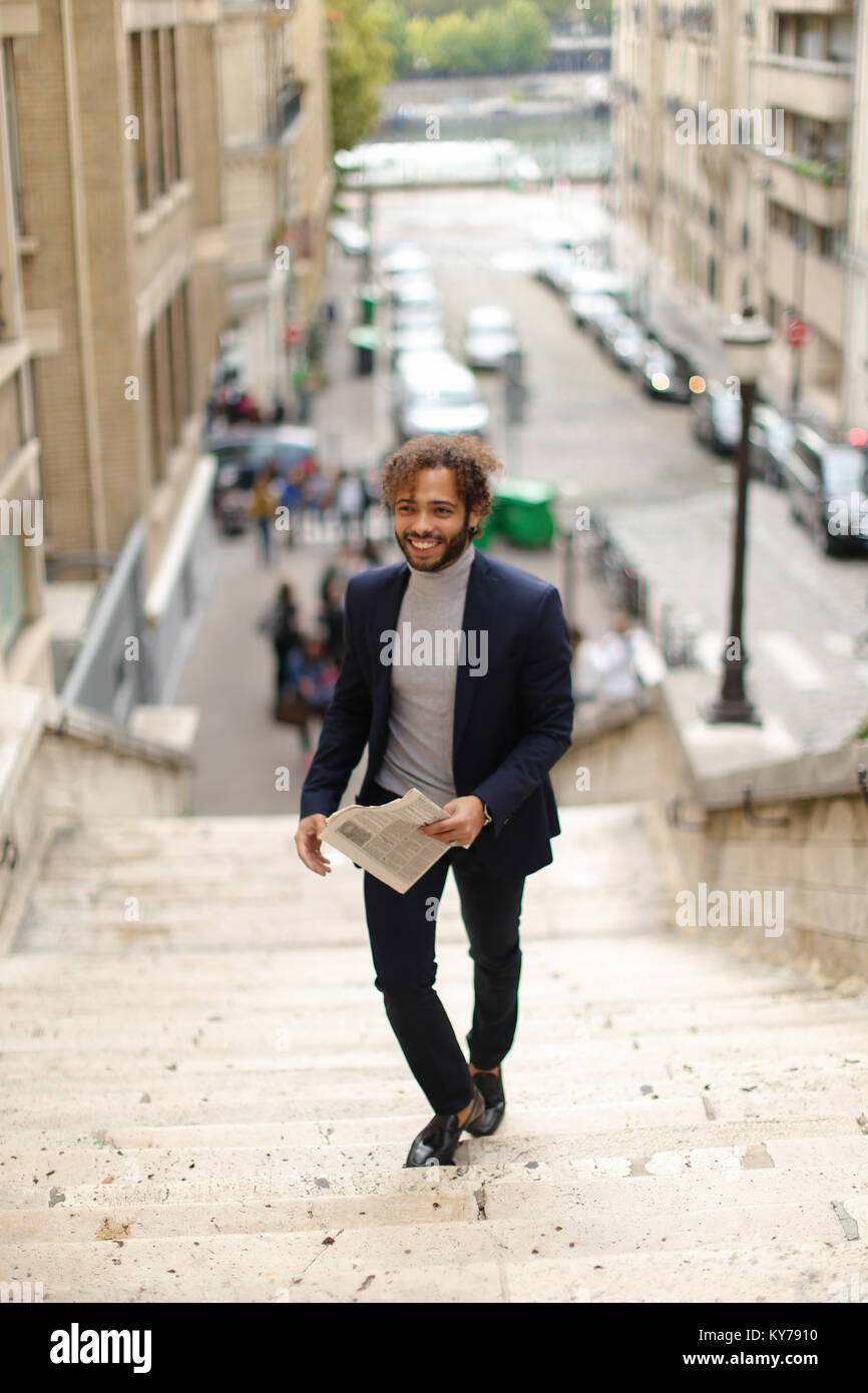 Young mix blood guy with newspaper walking down steps. Attractive male ...