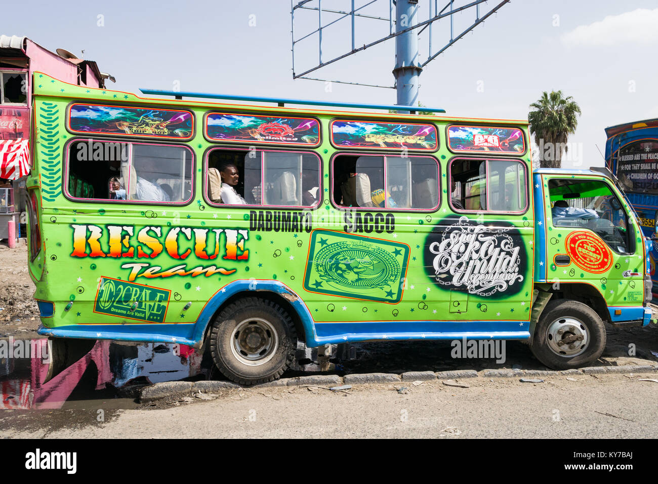 A brightly coloured bus with passengers waits on the road in traffic ...