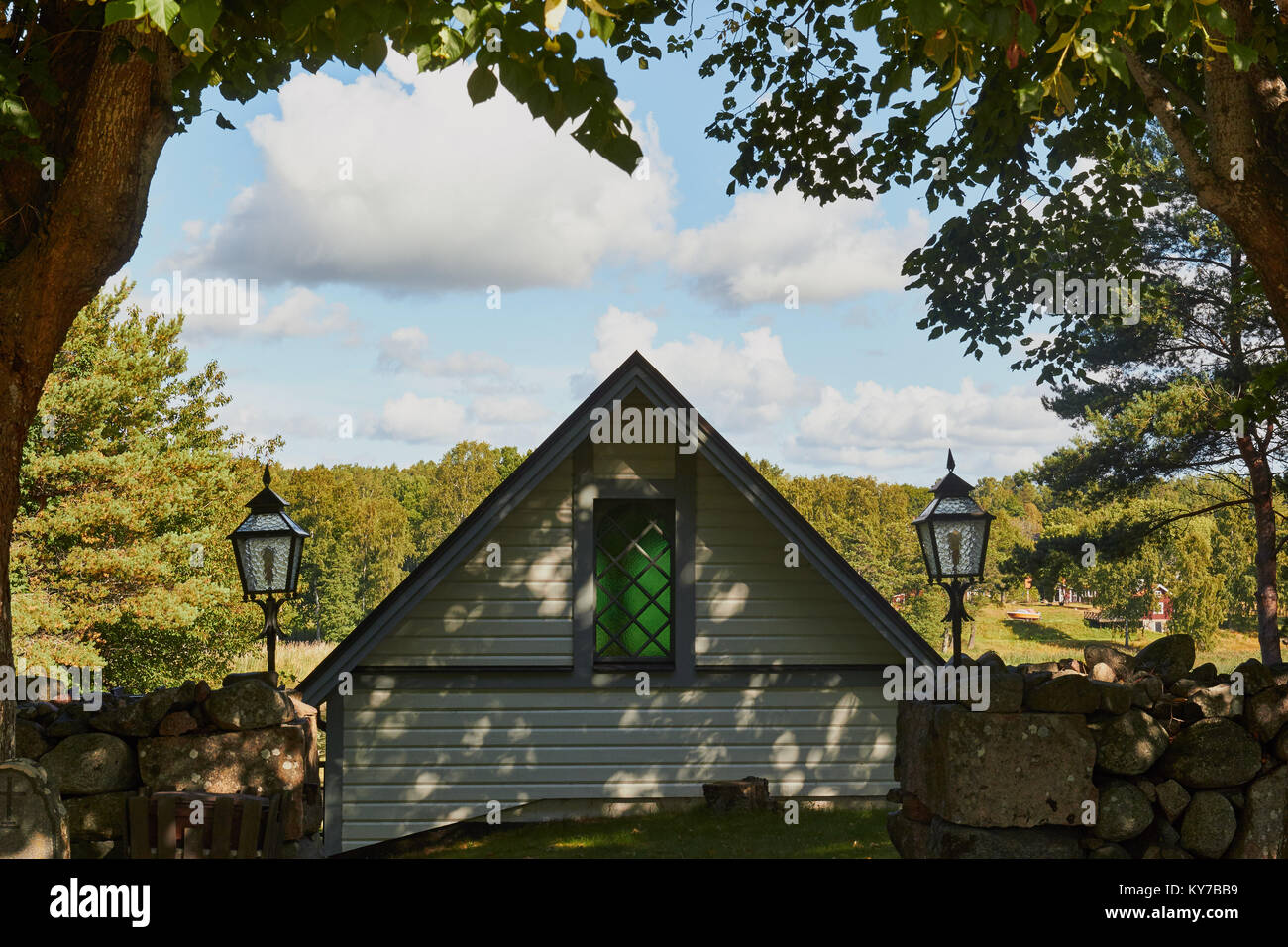Tiny wooden chapel shaded by trees in the grounds of Ljustero Church ...