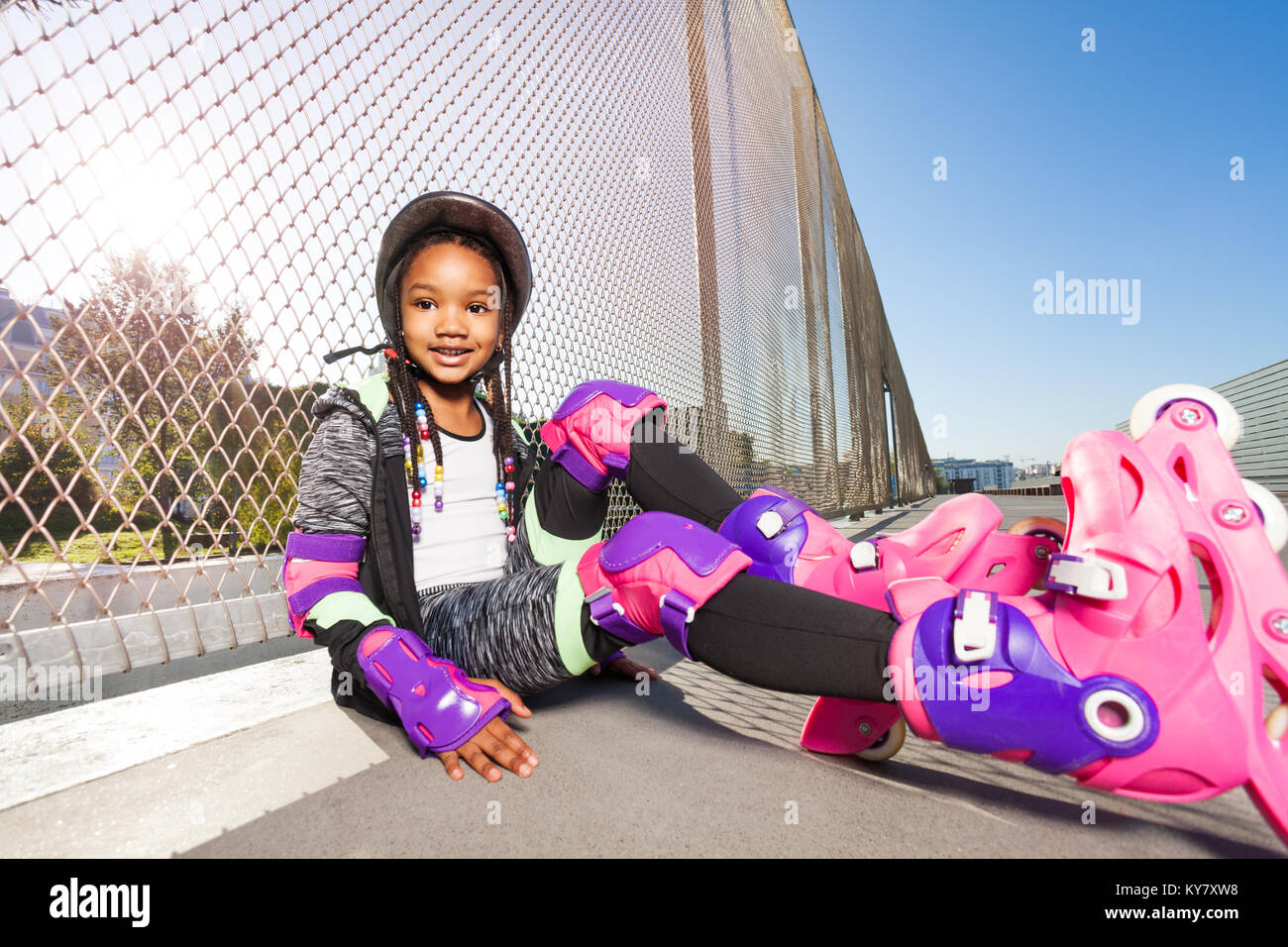 Portrait of African girl, smiling inline skater, sitting on the floor ...