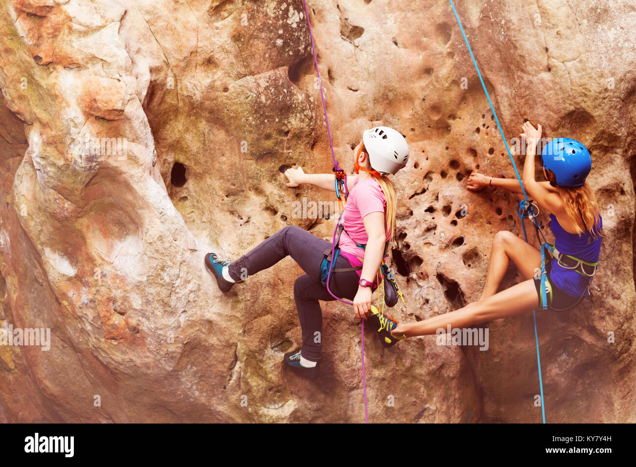 Back view of two rock climbers climbing up the hill with harnesses ...