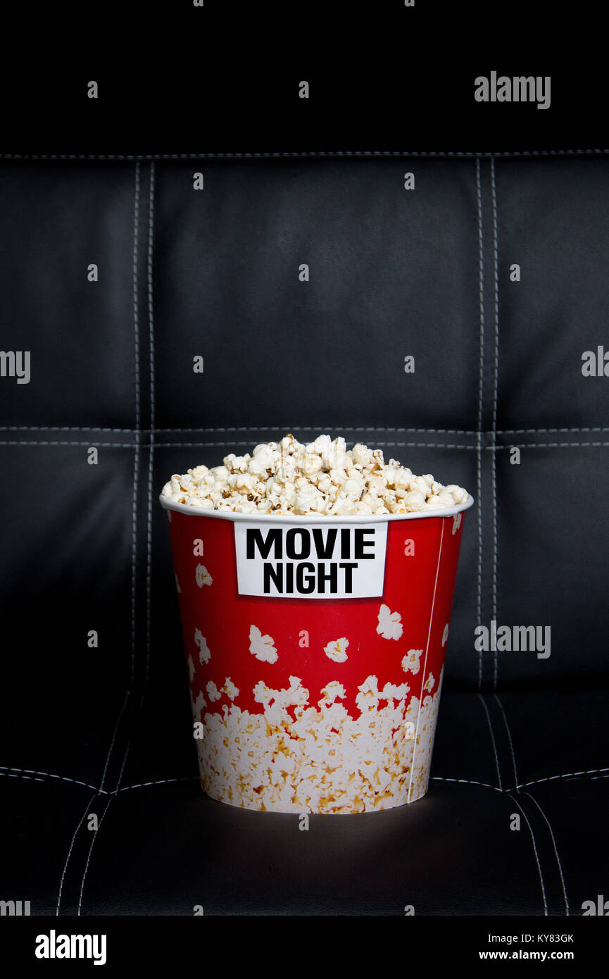 Closeup of a popcorn box on a black leather couch with black background ...