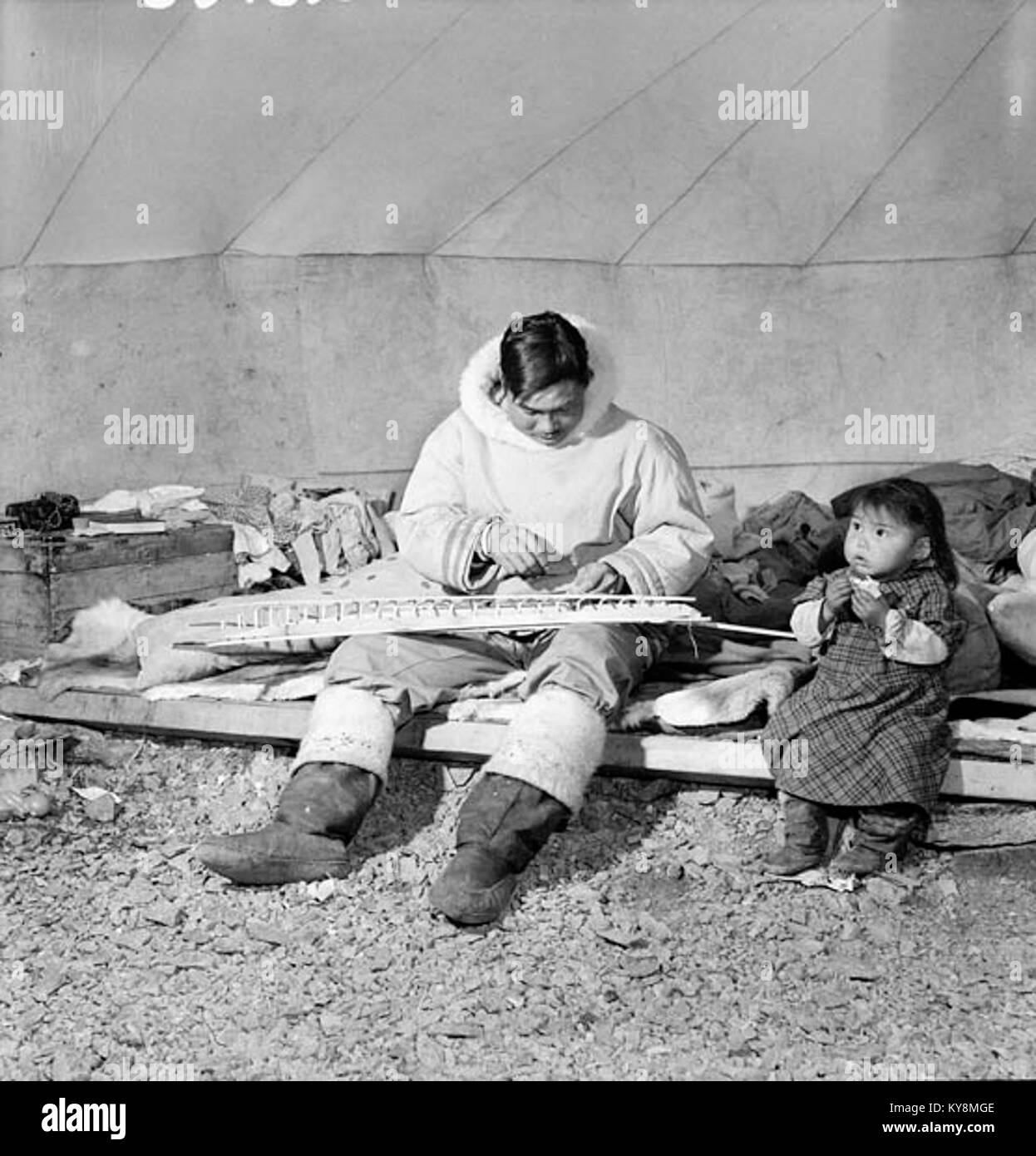 A 1951 photograph of Solomonie working on a model kayak in Cape Dorset ...