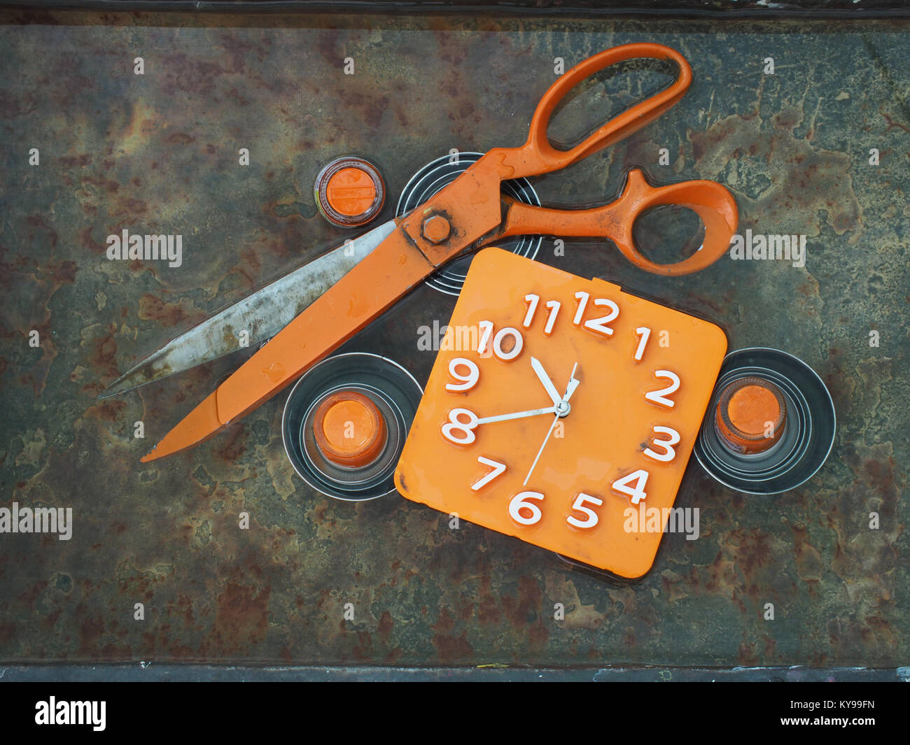 Orange scissors of large size next to the orange clock with a square ...