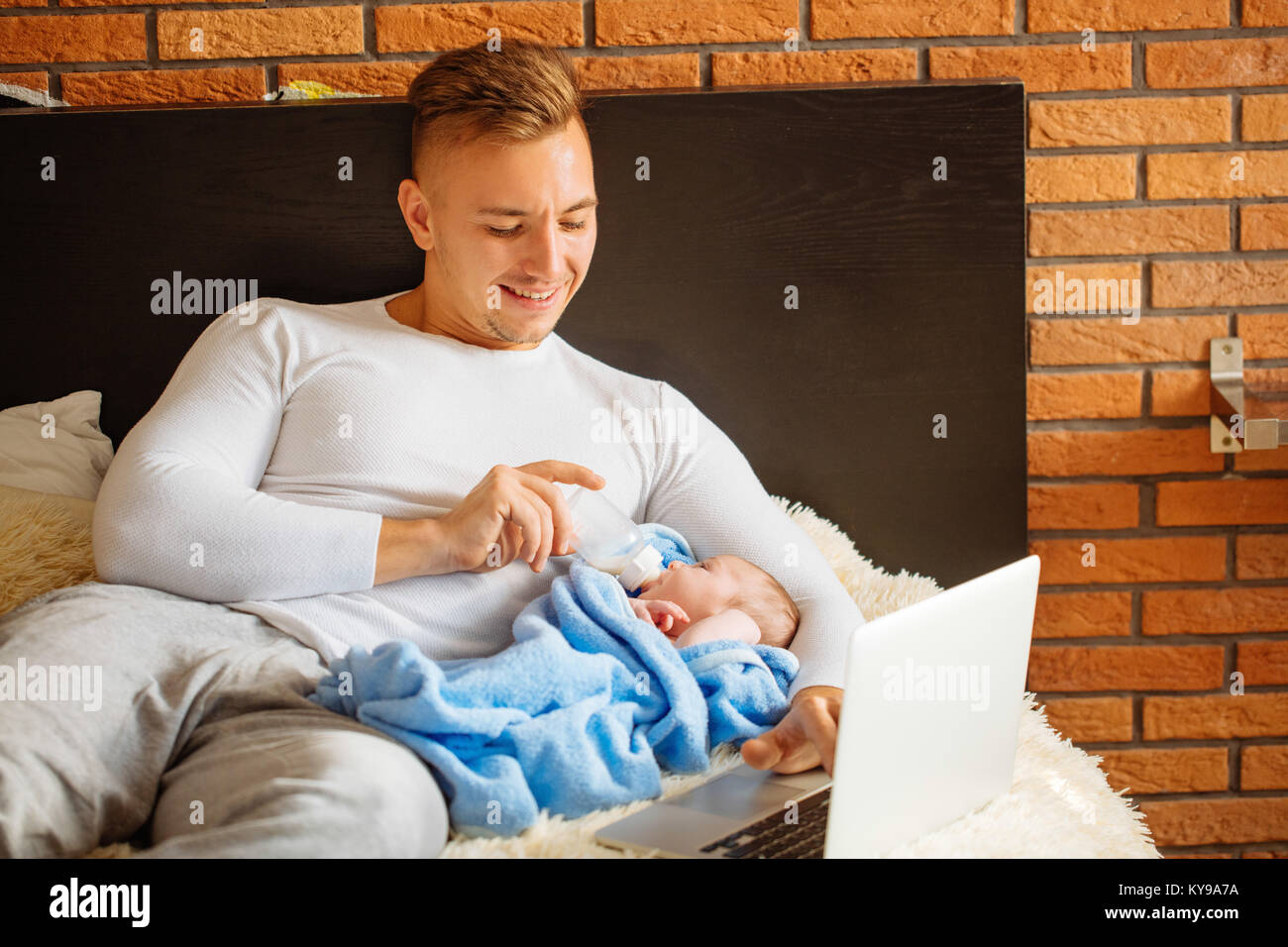man feeding little baby while lying on bed and working on laptop Stock ...