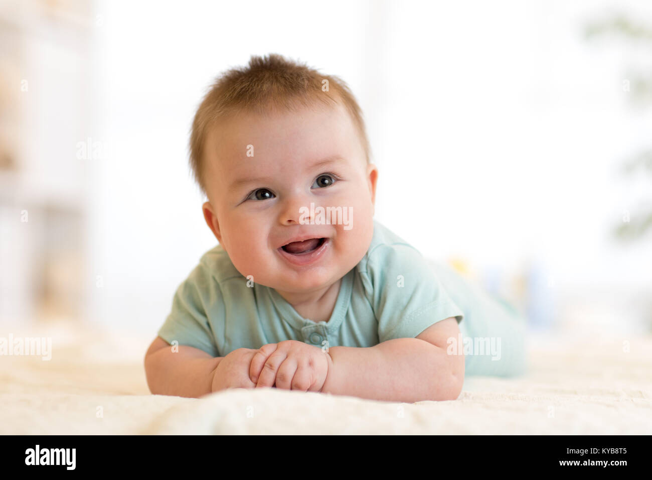Very happy laughing newborn baby in blue clothes lying on his belly ...