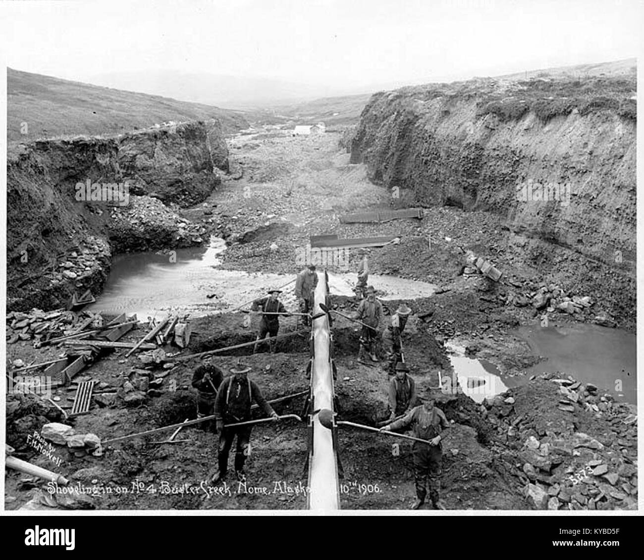 In 1906, men are shoveling dirt into a flume at a mining operation near ...