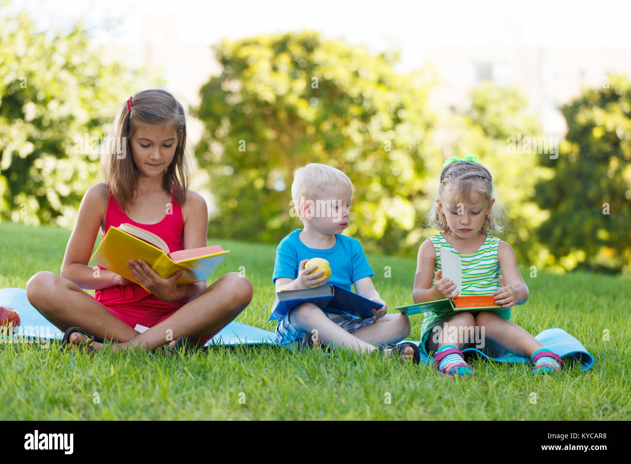 Three reading kids on the grass Stock Photo - Alamy