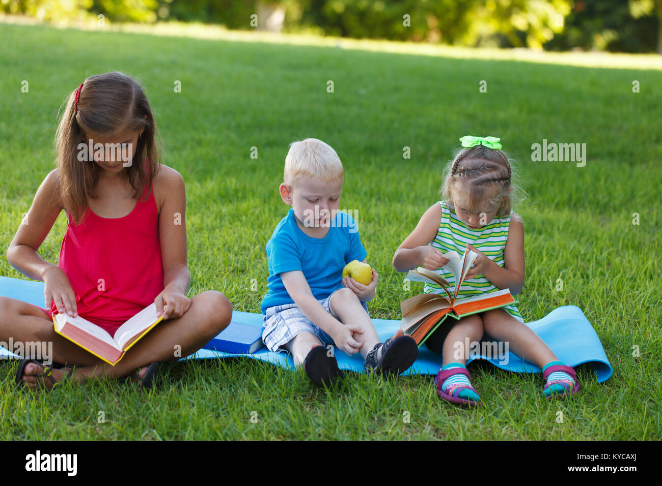 Three reading kids on the grass Stock Photo - Alamy