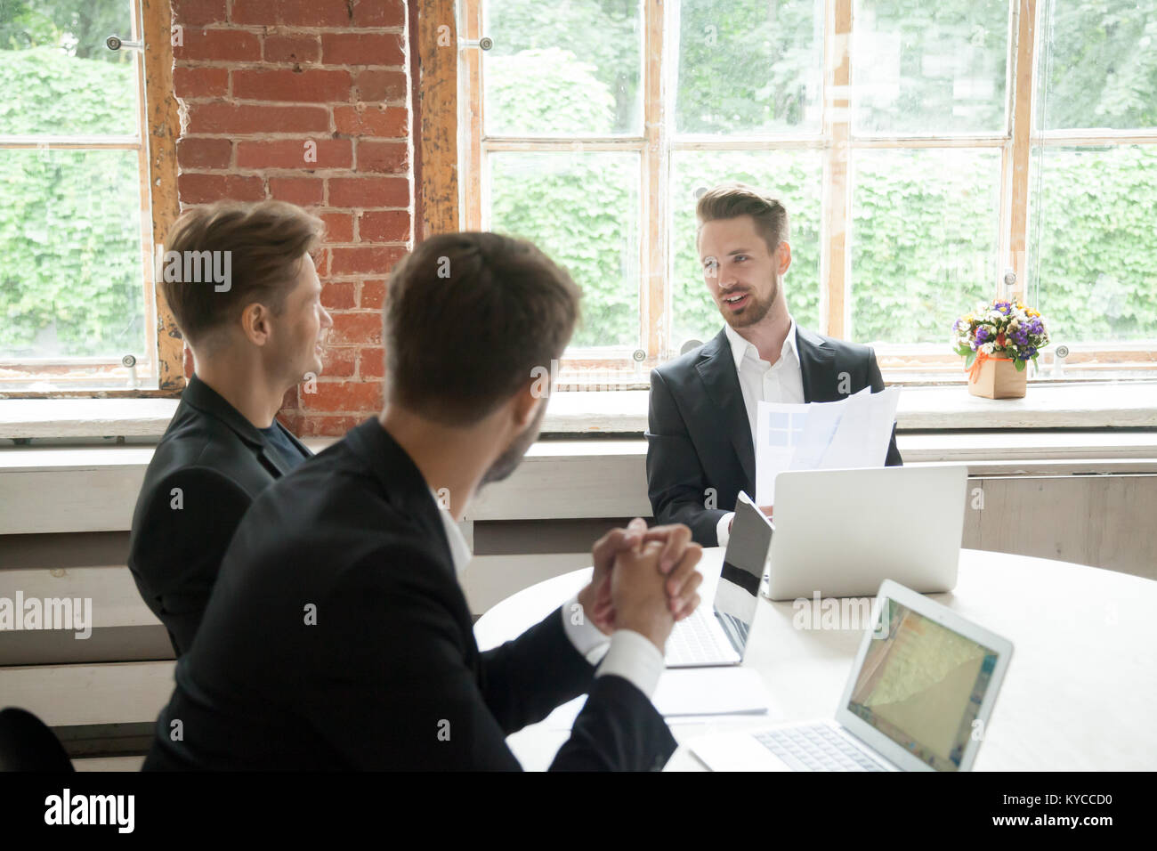 Three businessmen negotiate at meeting in boardroom, art director ...