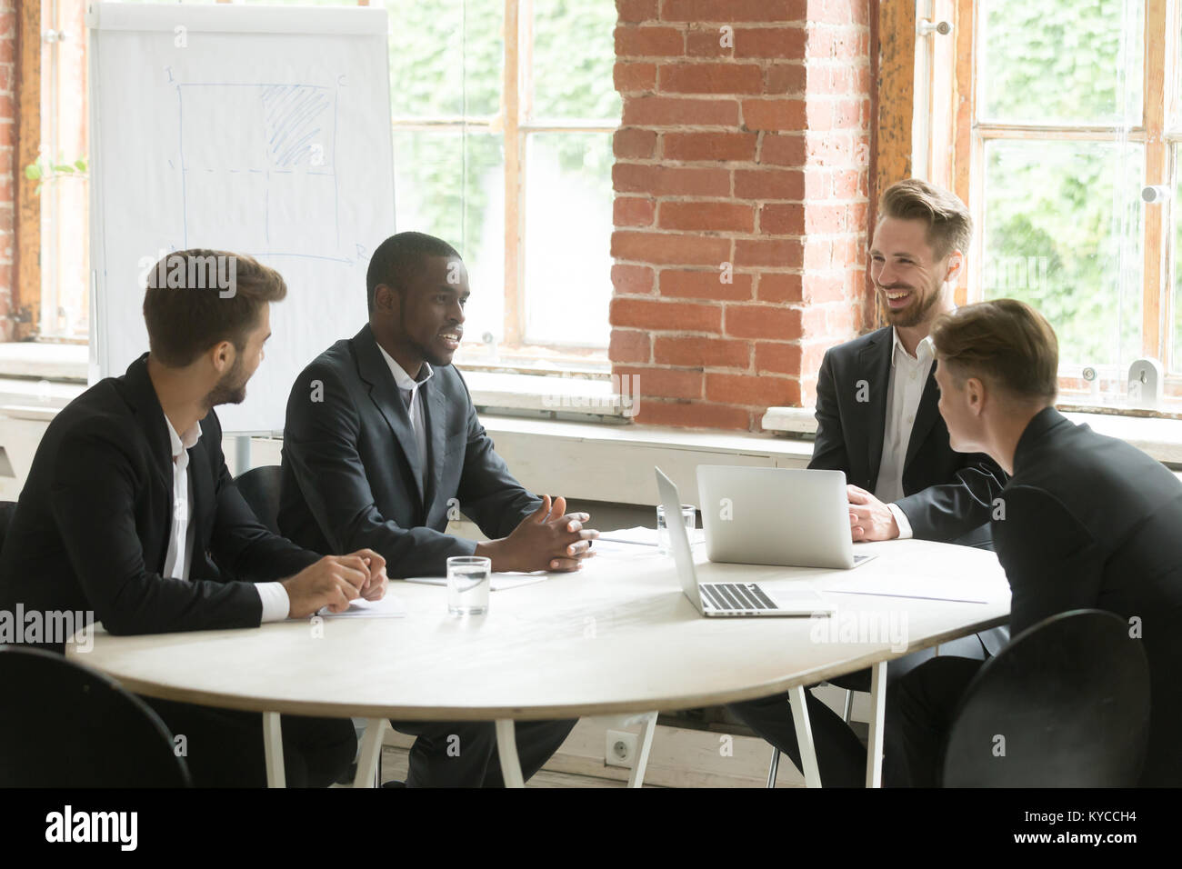 Four cheerful diverse businessmen talking laughing at meeting table ...