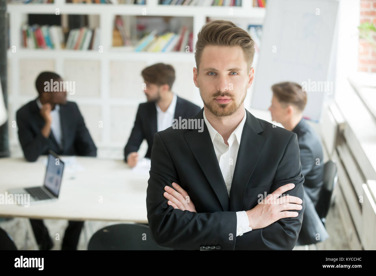 Serious young leader in suit looking at camera standing arms crossed on ...