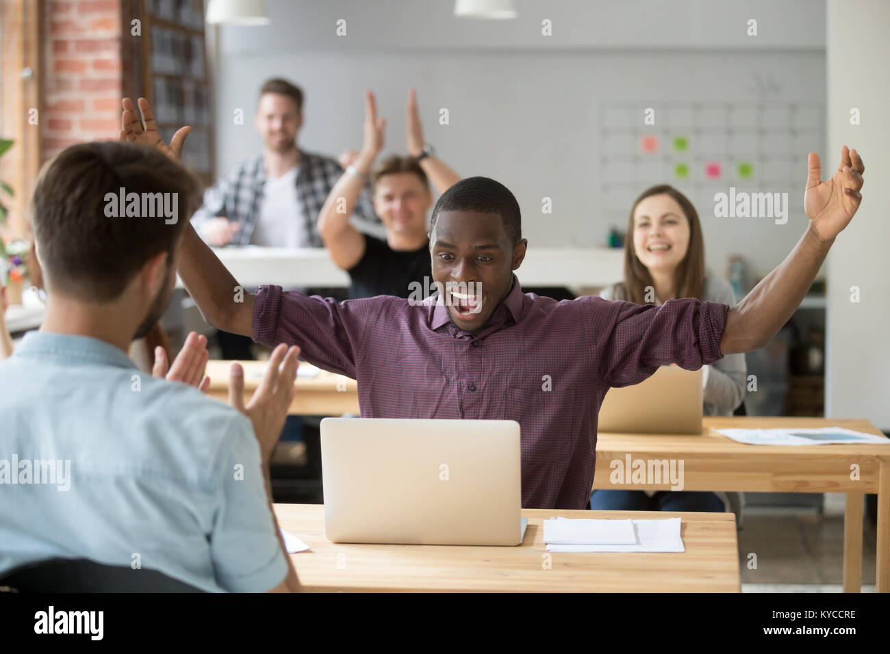 African employee excited about win online raising hands looking at ...