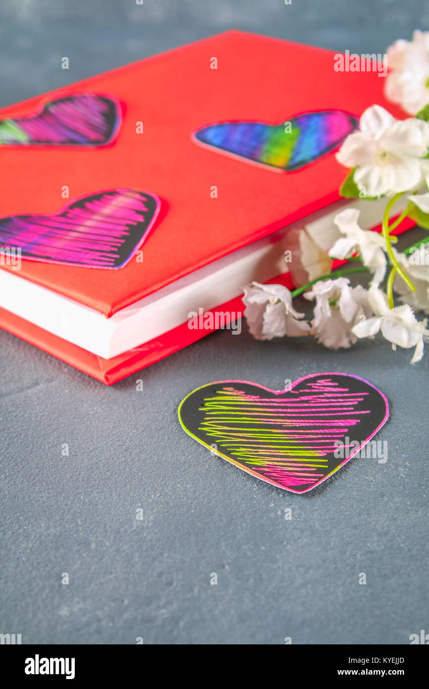 Black and pink hearts on a book in a red cover and flowers on a gray ...