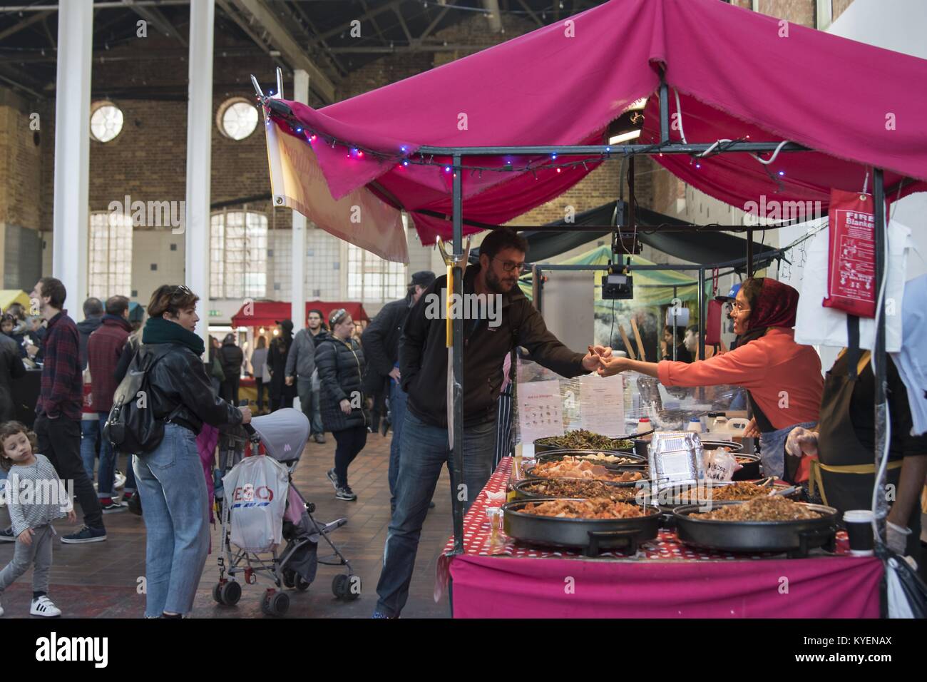 A vendor hands a food sample to a man at the Brick Lane Market, a major ...