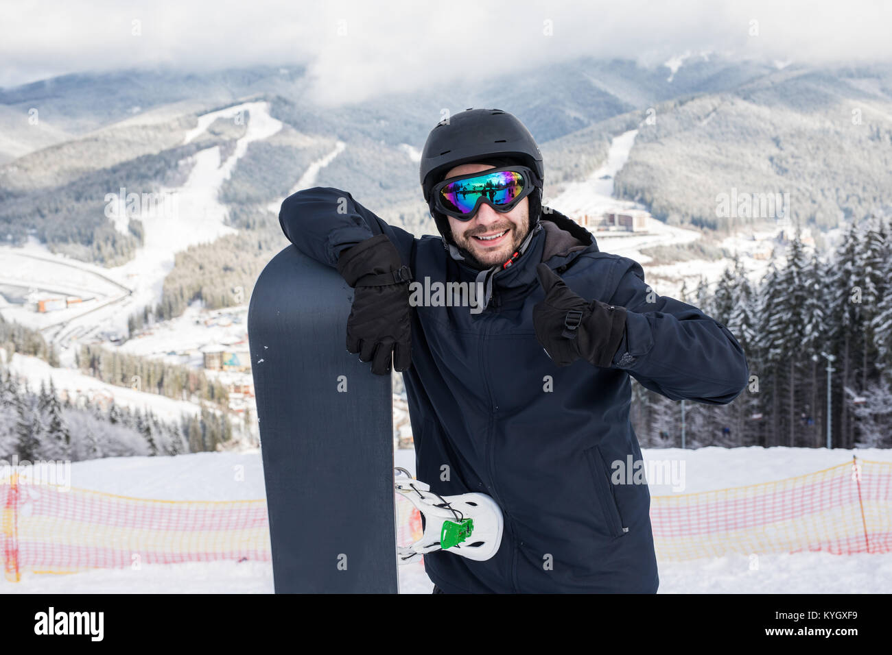 Man snowboarder standing on the top of the snowy slope with snowboard ...