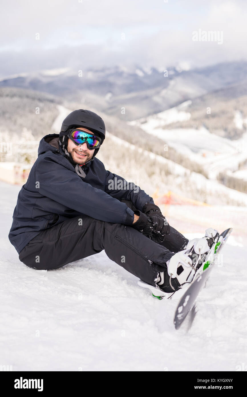 snowboarder sits high in the mountains on the edge of the slope and ...