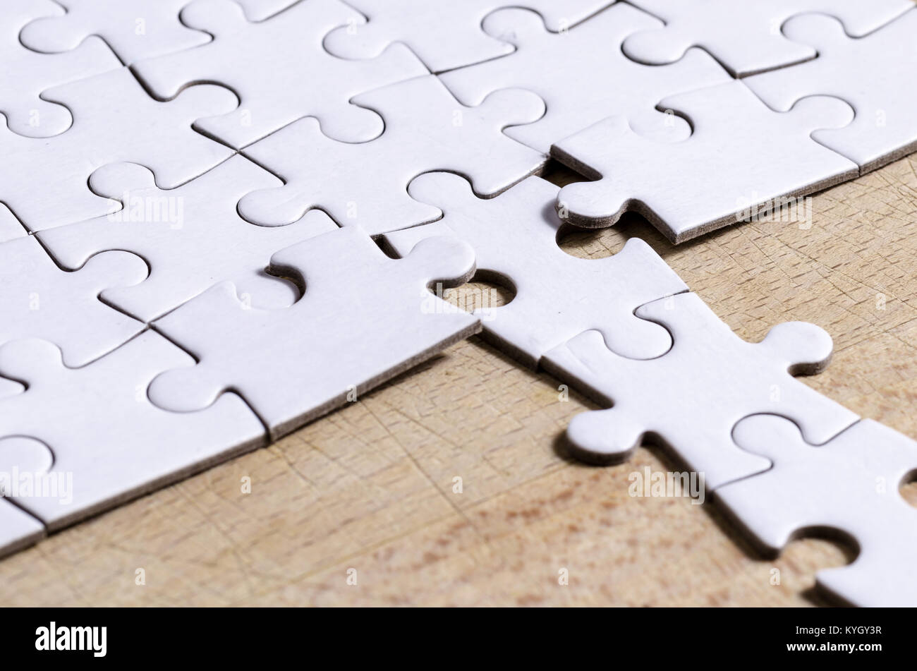 white jigsaw/puzzle with a row in wrong position, over wooden table ...