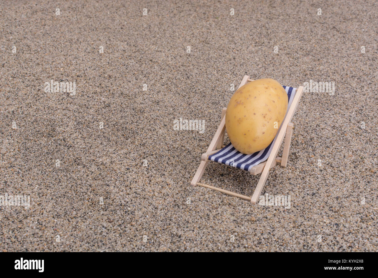 New potato on toy deckchair on sand - as visual metaphor for concept of ...