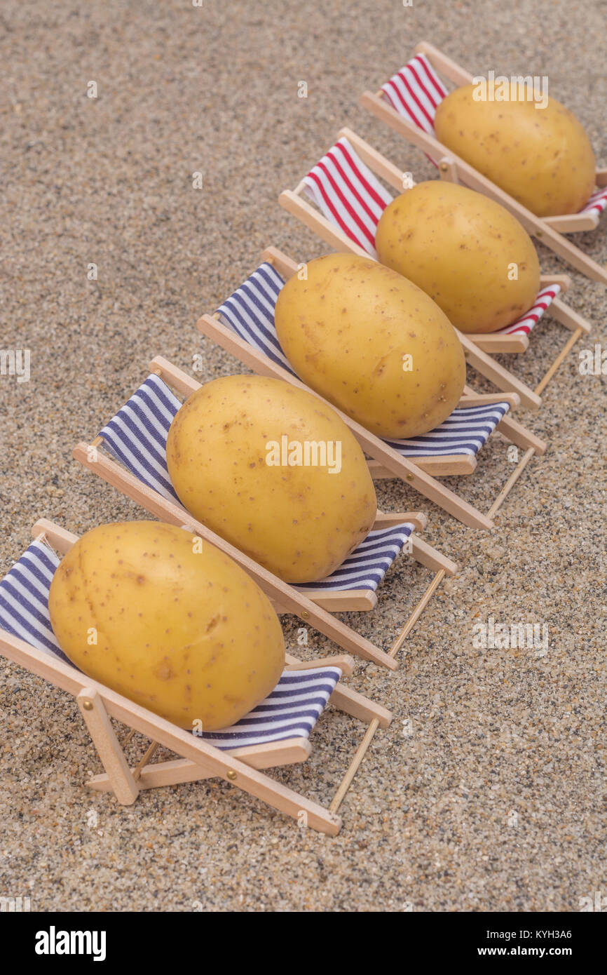 New potatoes on toy deckchairs on sand - as visual metaphor for concept ...