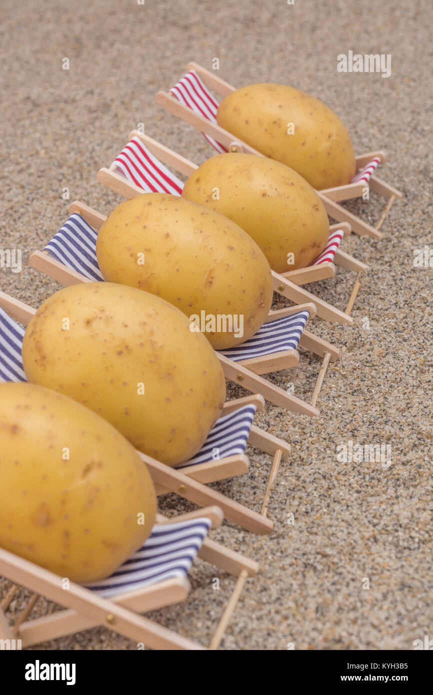 New potatoes on toy deckchairs on sand - as visual metaphor for concept ...