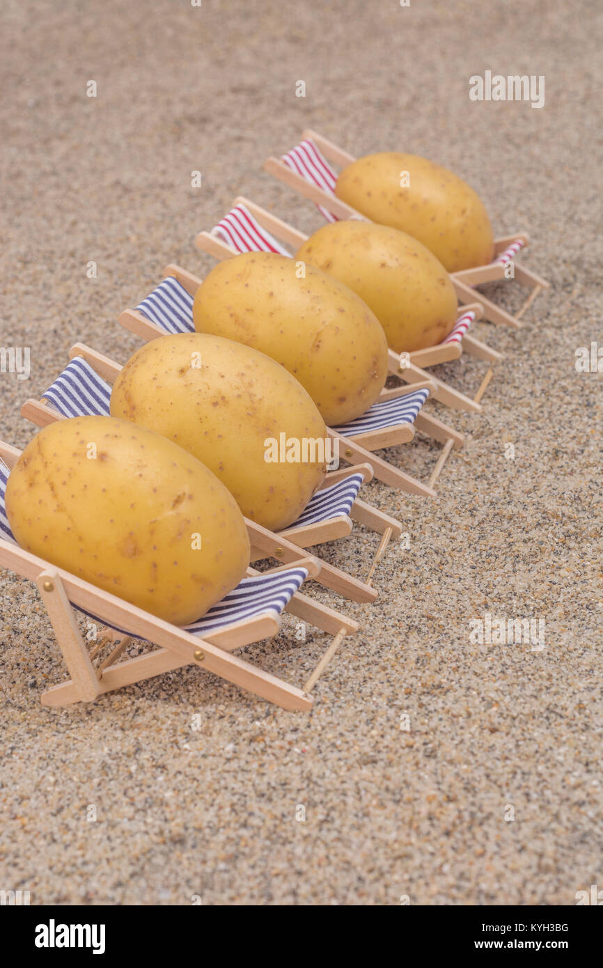New potatoes on toy deckchairs on sand - as visual metaphor for concept ...