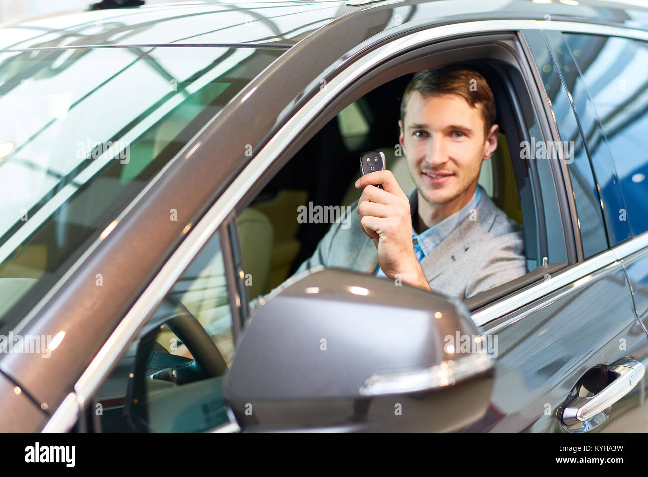 Portrait of handsome young man sitting inside of luxury car and holding ...