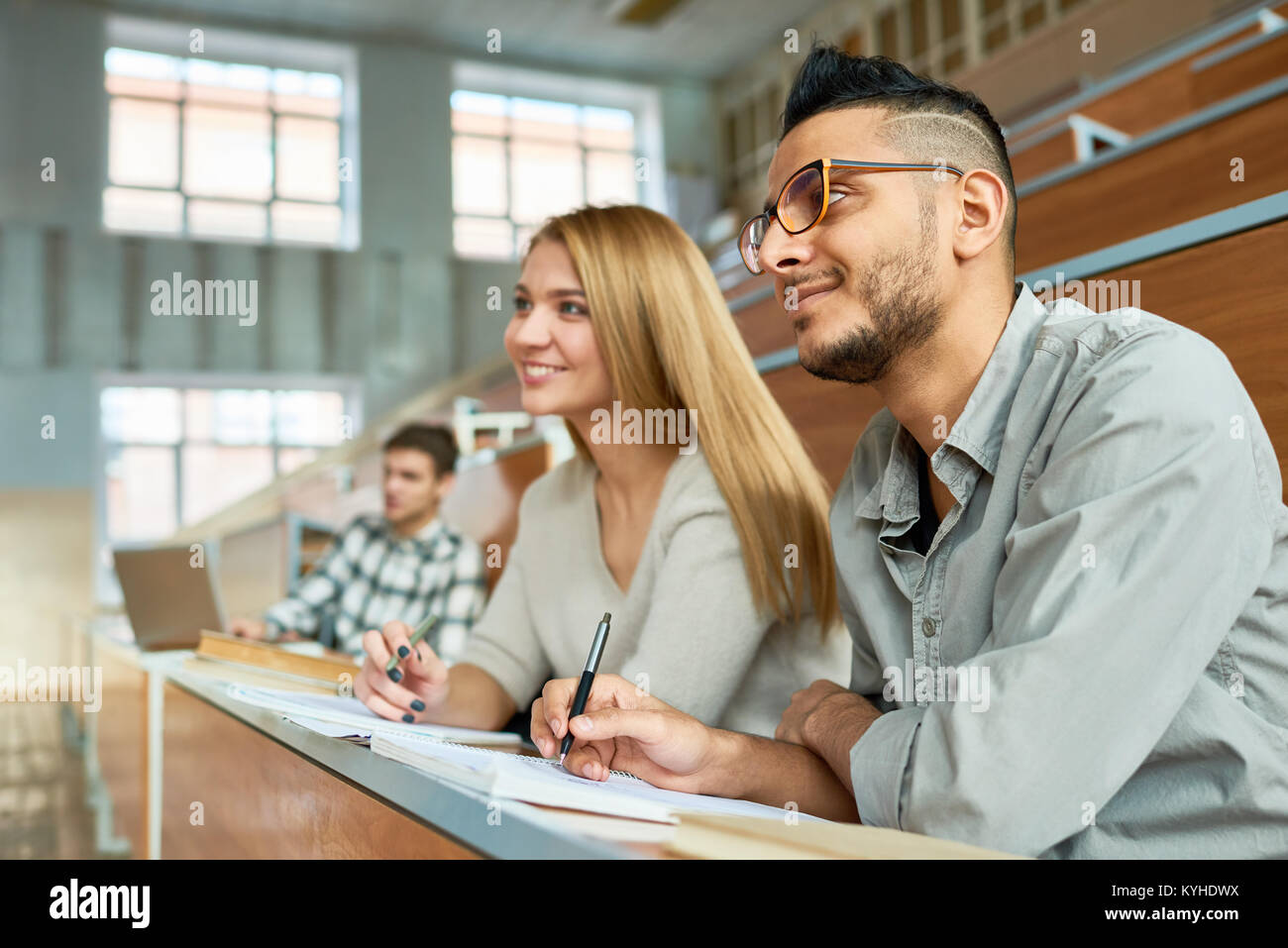 Multi-ethnic group of students sitting at desk in lecture hall of ...