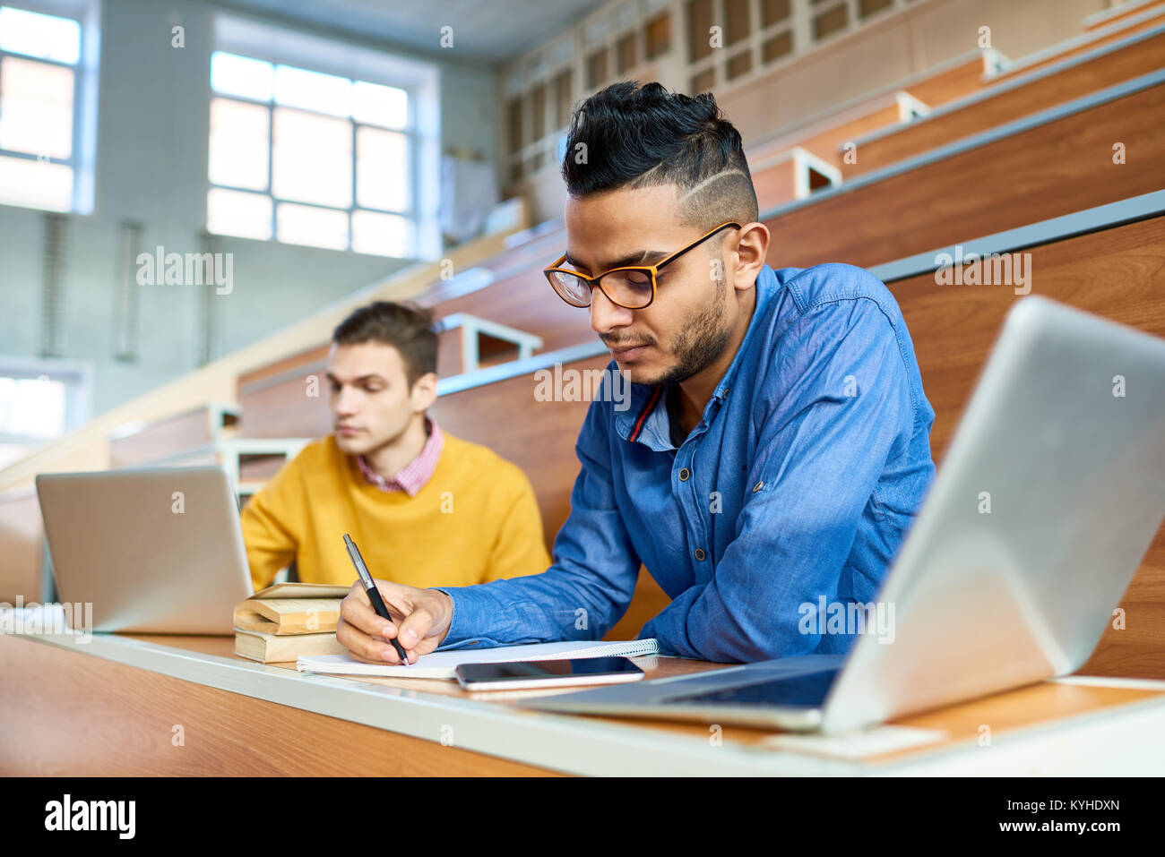 Portrait of two students sitting at desks in modern auditorium at ...