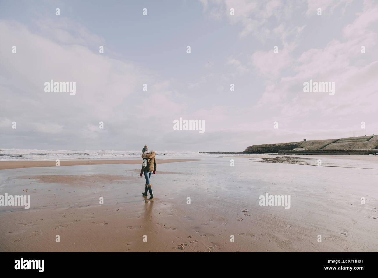 A young woman walks alone on a winter beach in Tynemouth whilst facing ...
