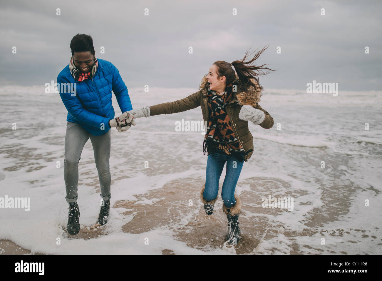 A young couple laugh, hold hands and paddle in the sea on Tynemouth ...