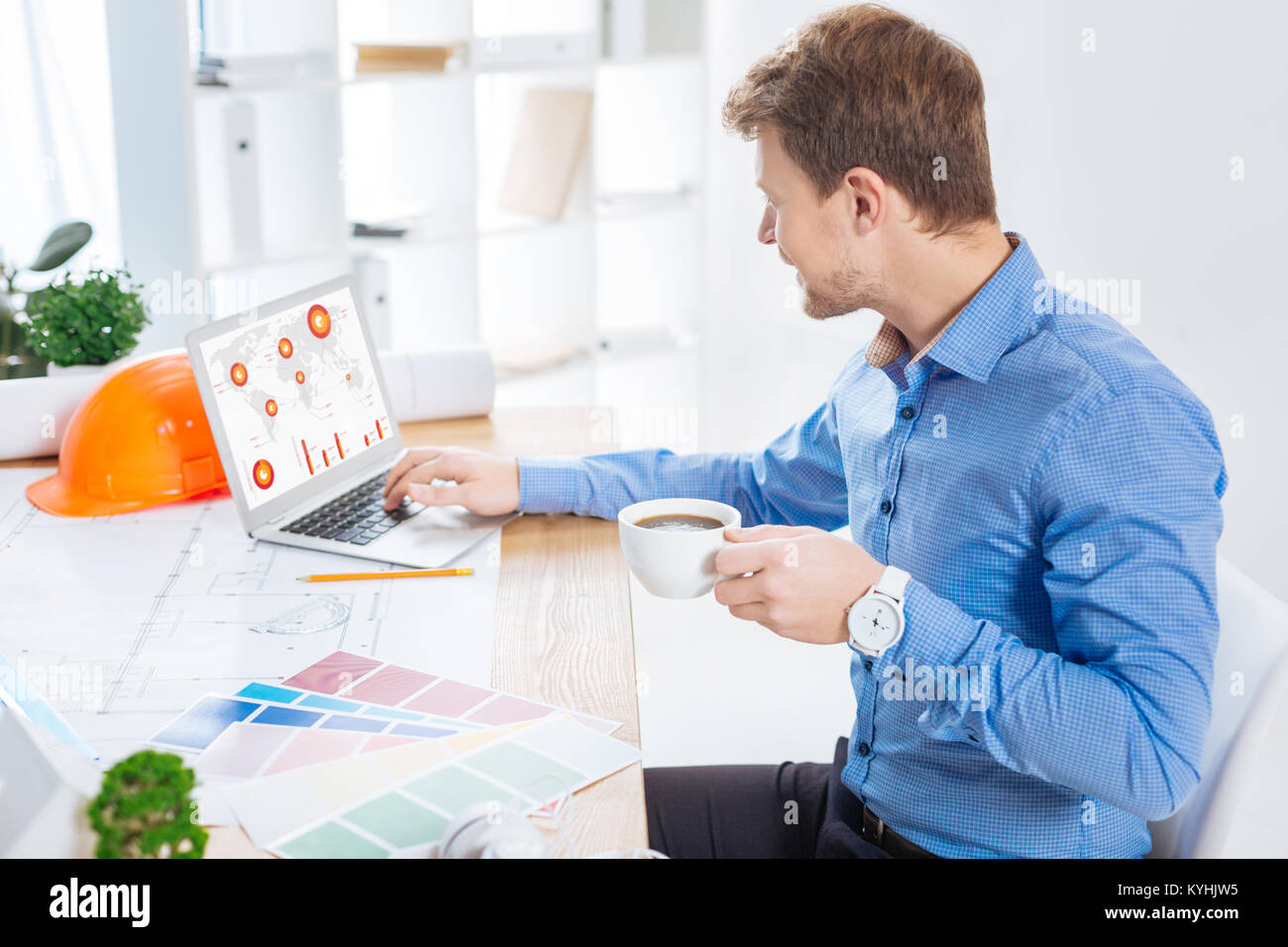 Smart young engineer looking at the screen while drinking his coffee ...