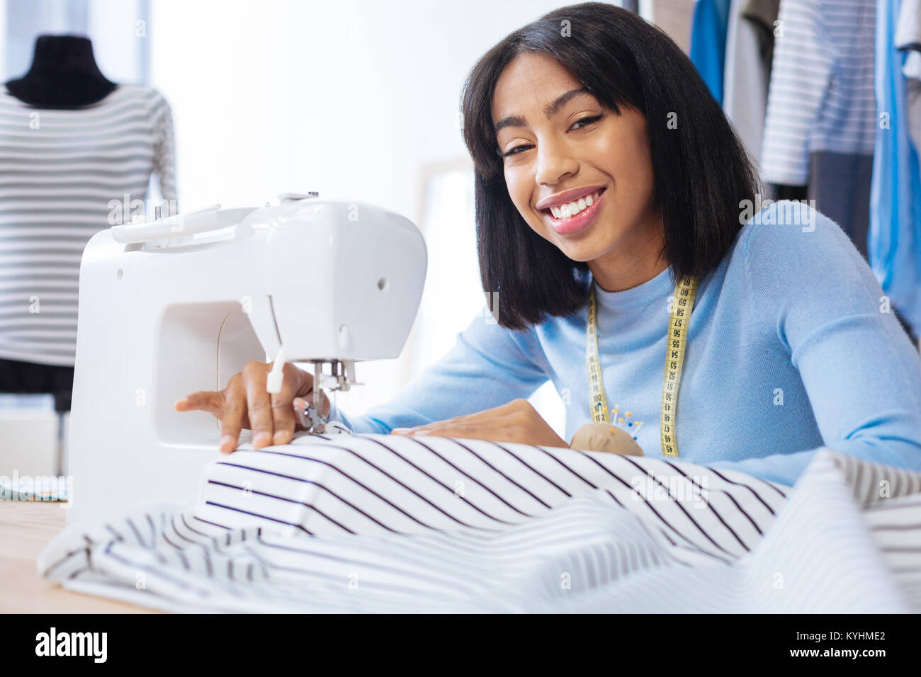 Happy worker of tailor house smiling while sewing a blouse Stock Photo ...