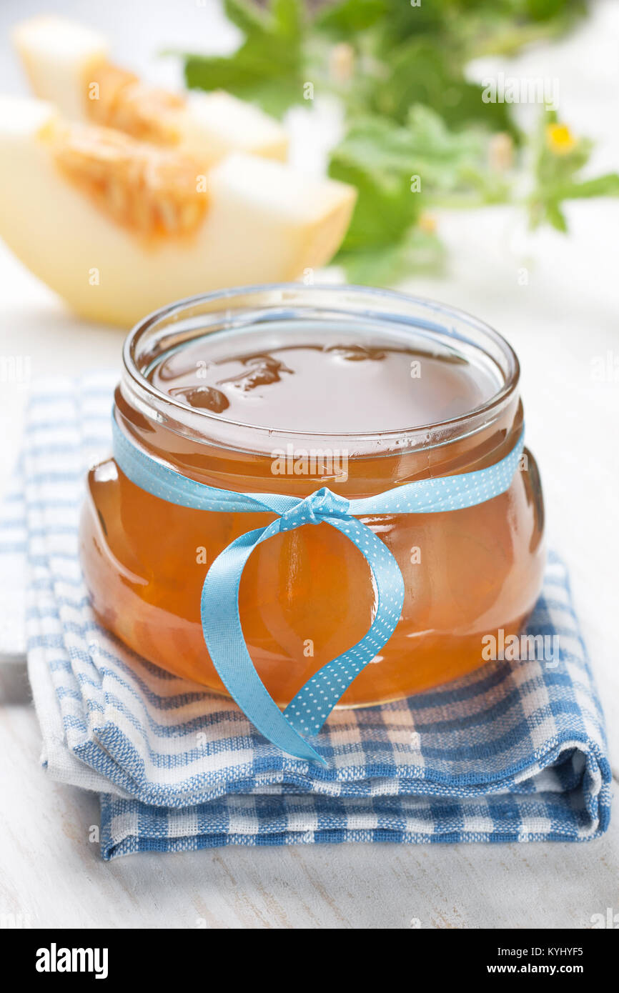 jam melon in a glass jar, slices of melon on a white wooden background ...