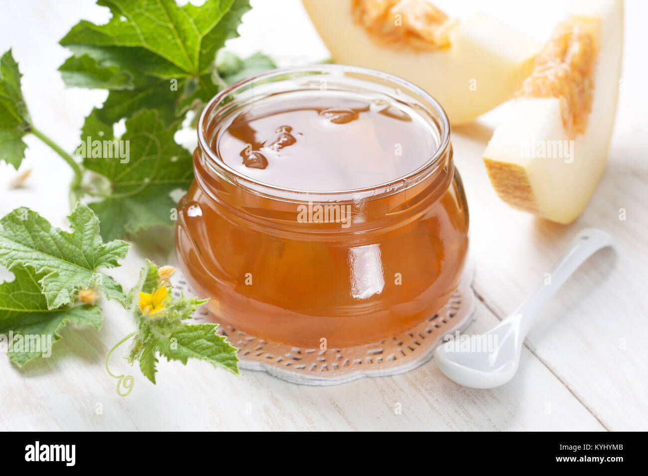 jam melon in a glass jar, slices of melon on a white wooden background ...