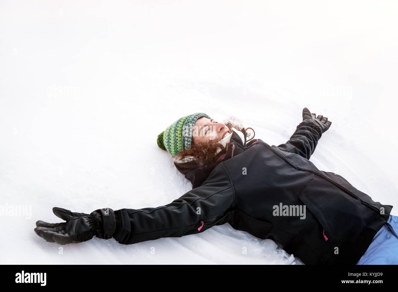 Joyful cheerful girl lying down on the white clean snow with raised up ...