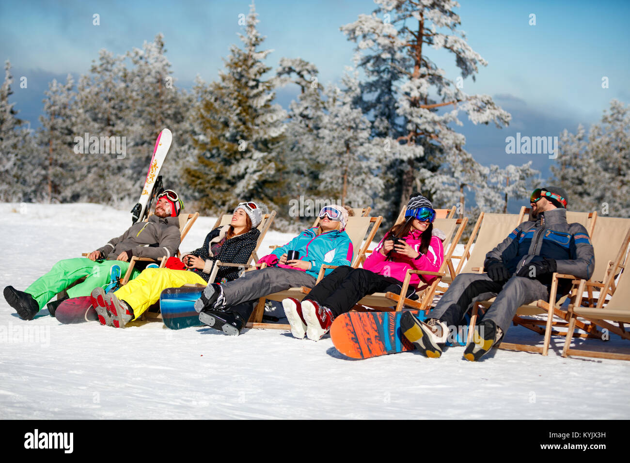 Group of friends sitting with deck chairs in winter mountains ...