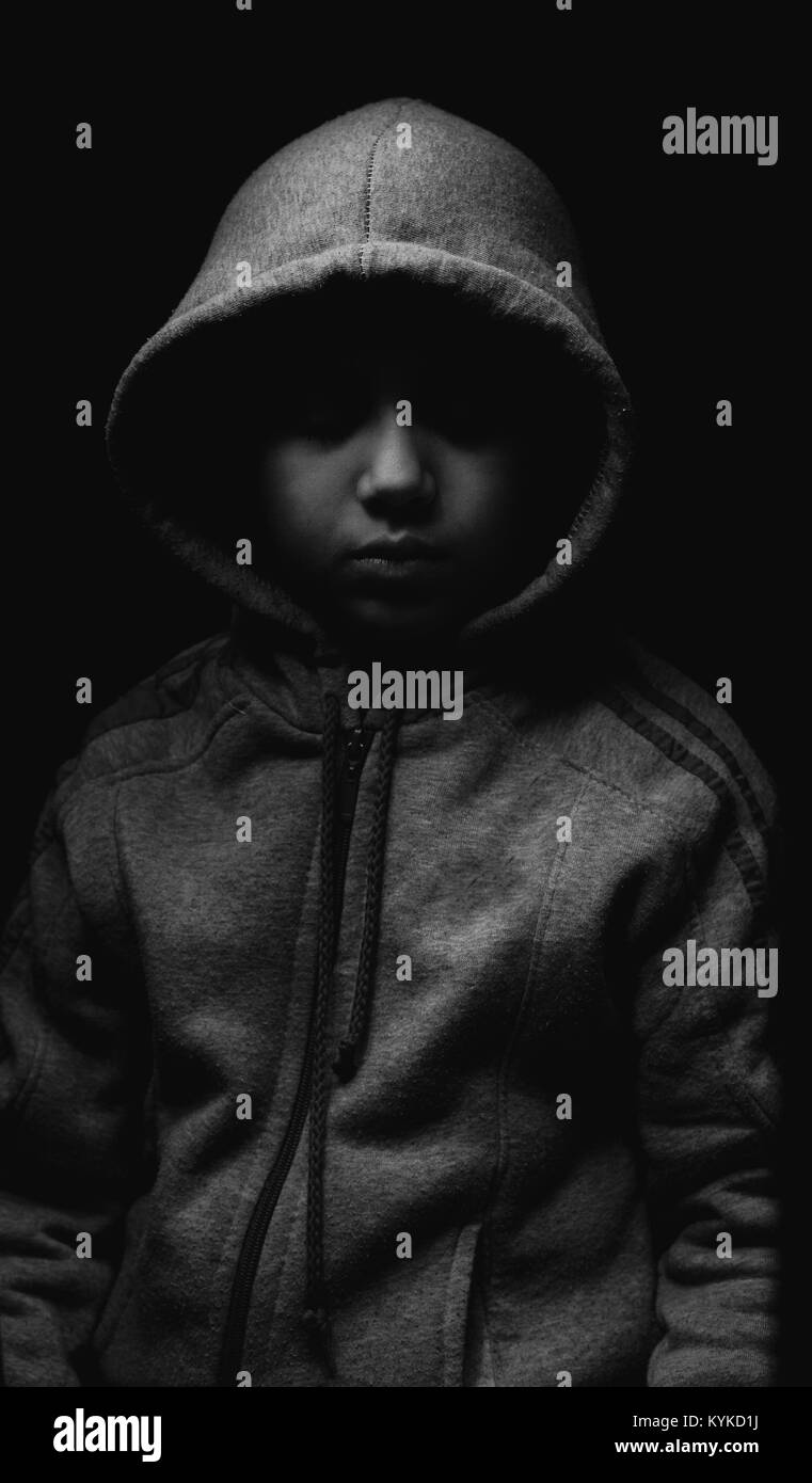 a black and white lowkey portrait showing a mysterious boy with a hood ...