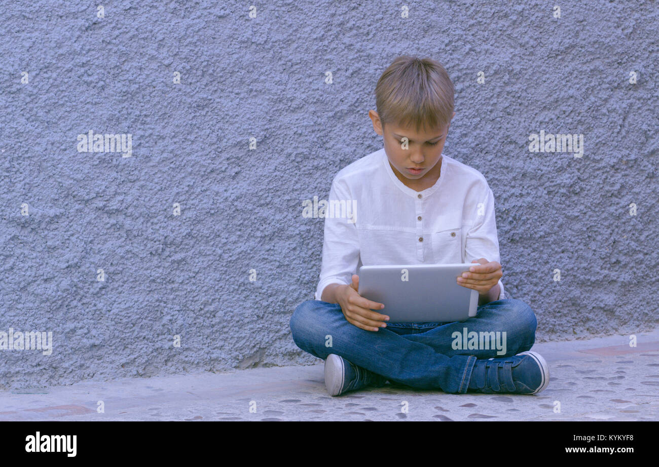 Child with tablet computer sitting on the ground outdoors Stock Photo ...