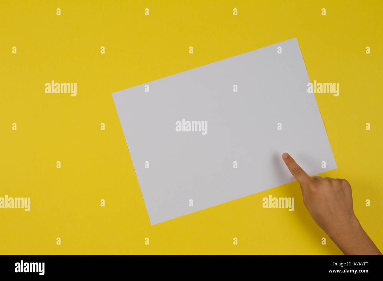 Kids hand finger pointing to white blank paper card on yellow ...