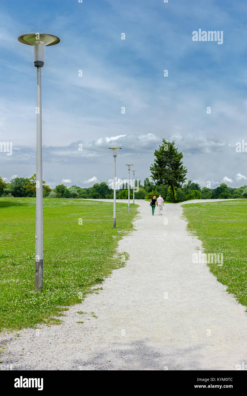 White path in a park leading in to the distance, with blue sky and ...