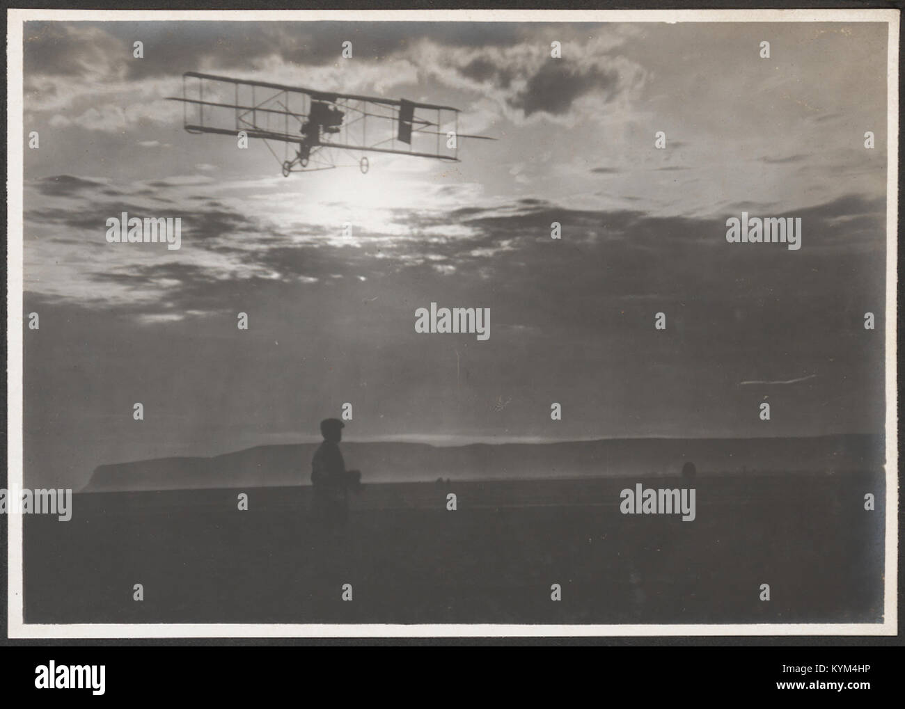 A biplane flying above with a man observing the aircraft from below ...
