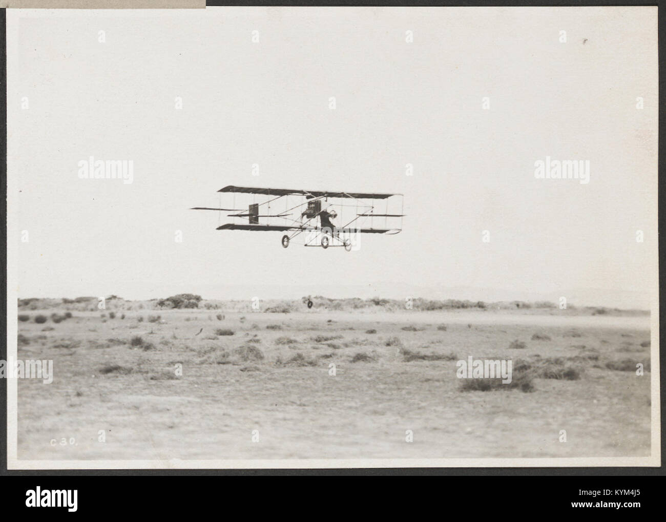 A photograph of a Curtiss Pusher biplane flying low over a field. The ...