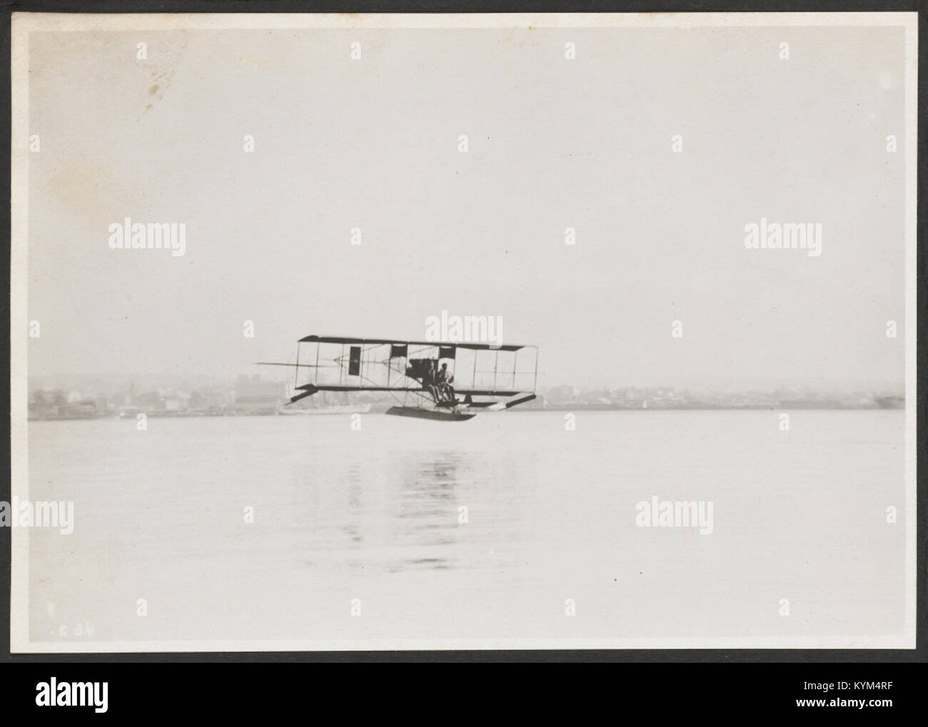 The Curtiss Pusher, an early biplane, is shown in flight over water ...