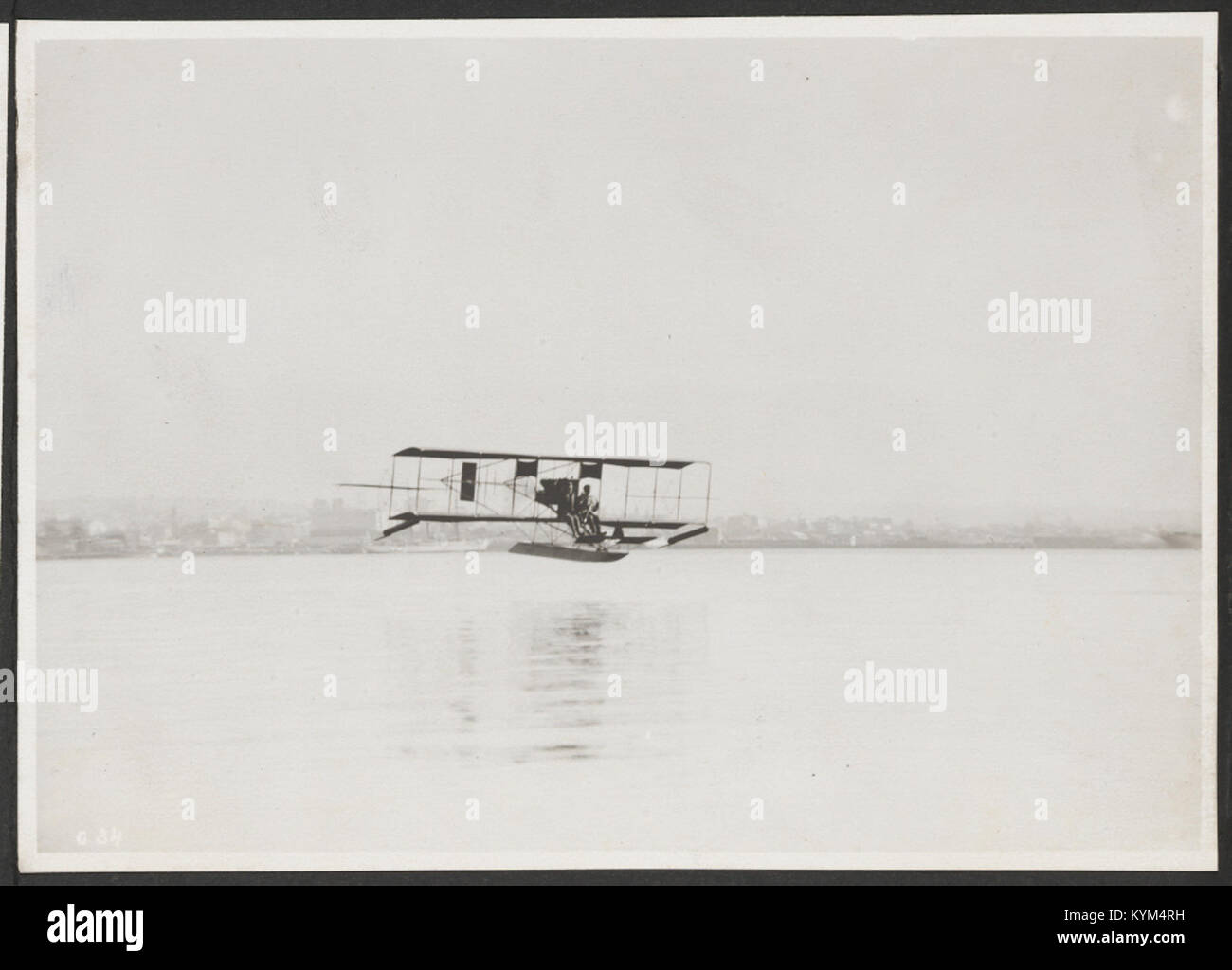 A Curtiss Pusher biplane in flight over water. The aircraft is an early ...