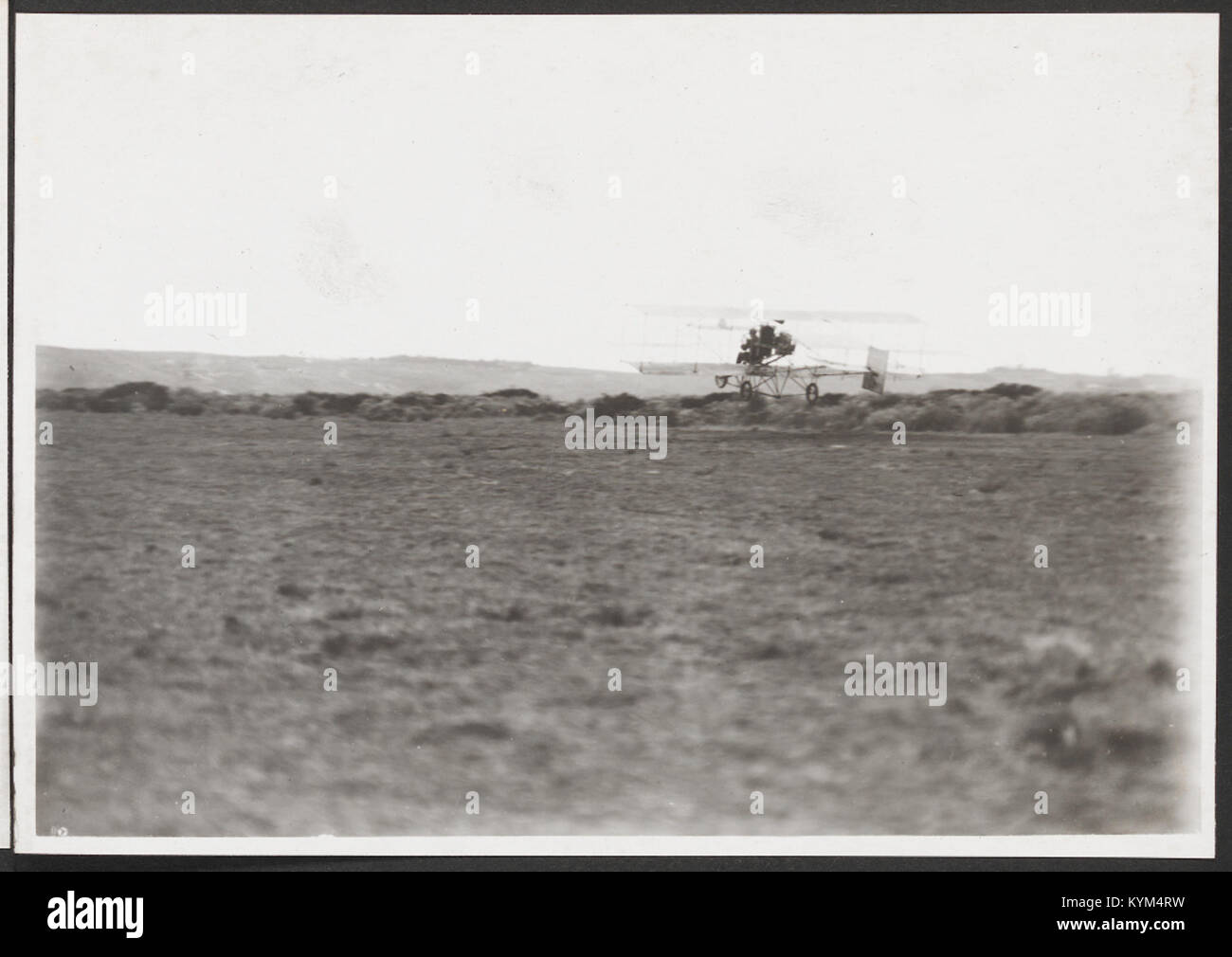 Biplane flying low over a field, captured in a vintage photograph. The ...