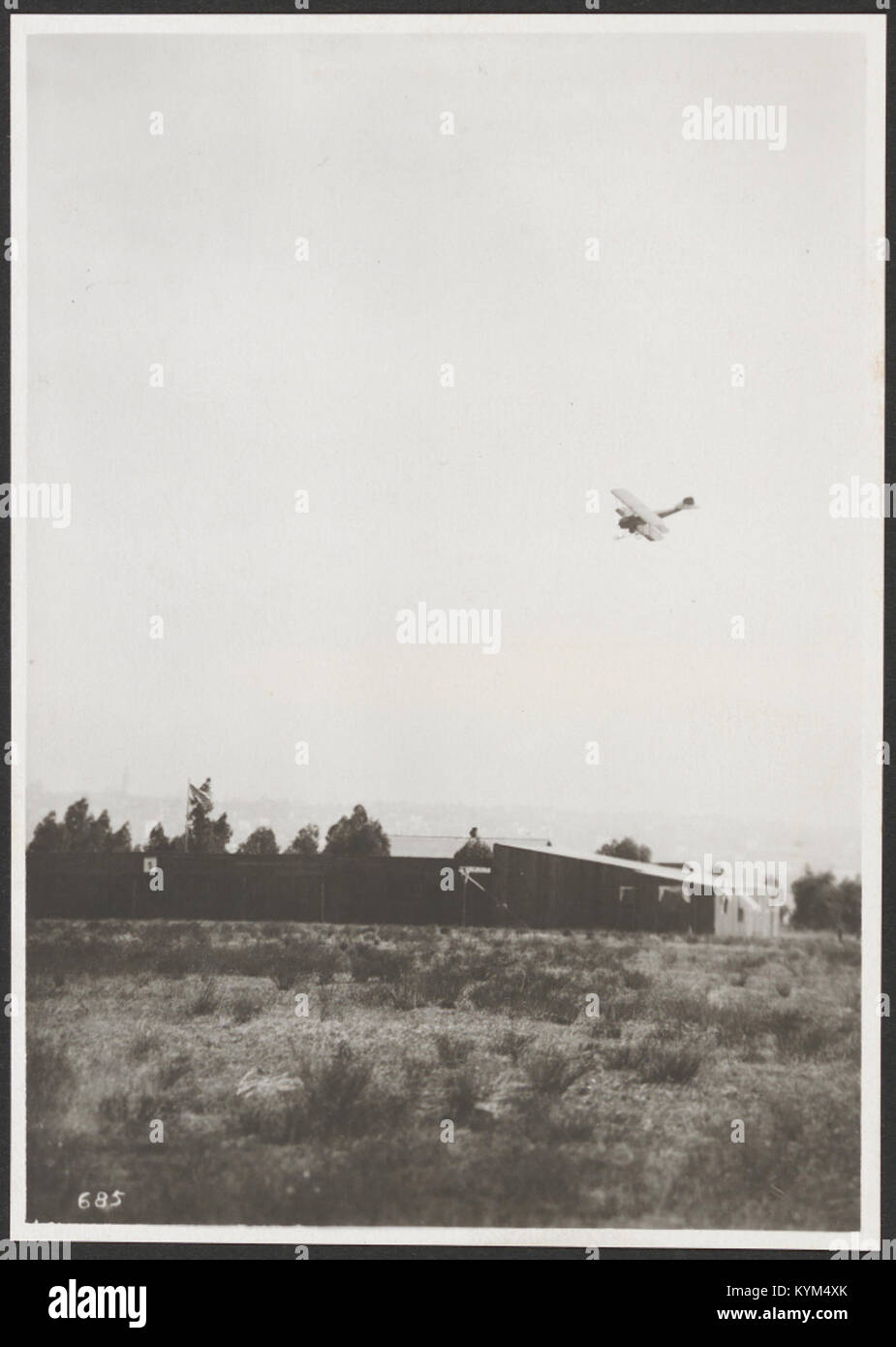 The Martin TT biplane in flight over a hangar, captured in an archival ...