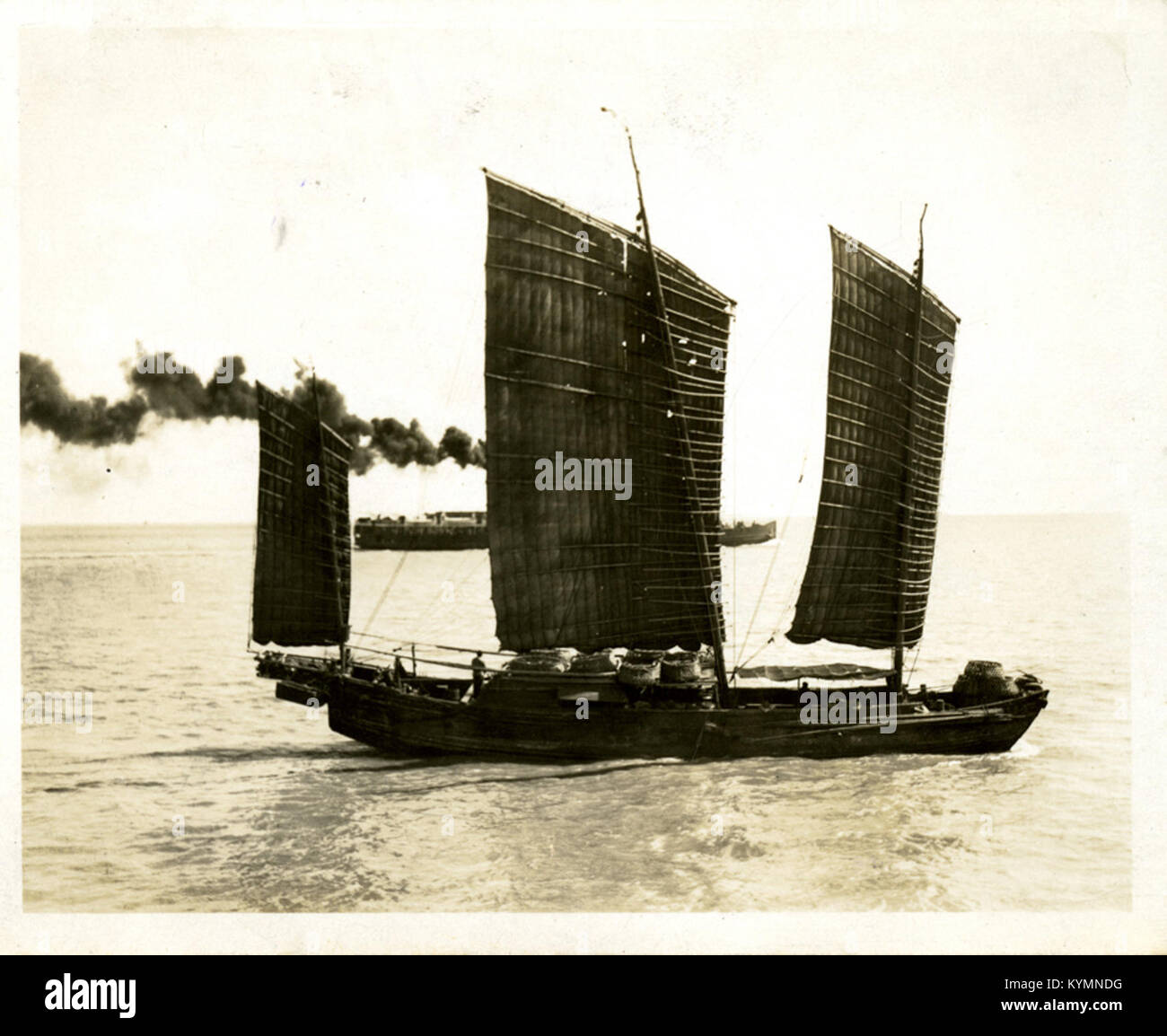 A historic photograph of a Chinese junk boat with a steamboat visible ...